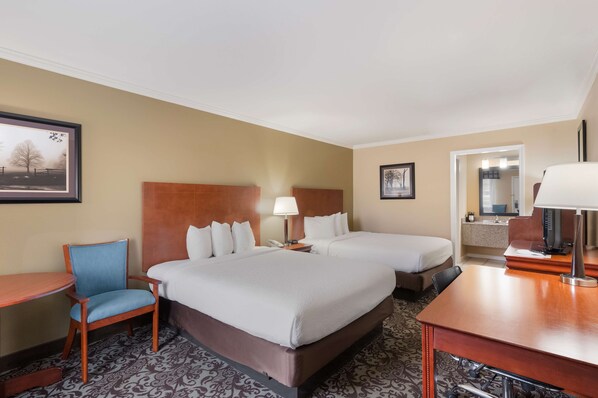 Quarto de hotel com duas camas, uma mesa, uma cadeira, um abajur e um quadro pendurado na parede.