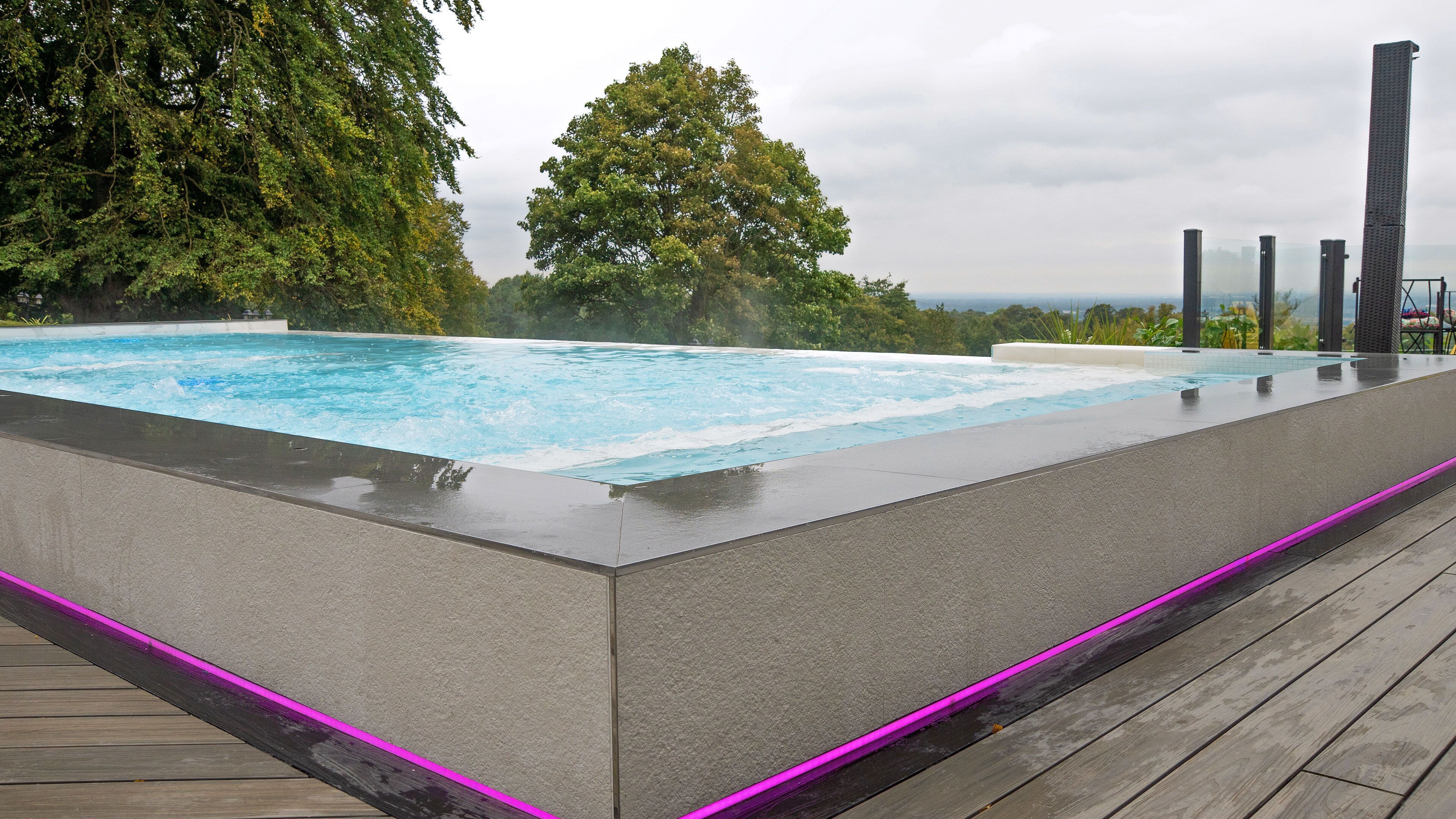 Uma piscina infinita moderna com vista para o oceano, cercada por vegetação exuberante e um deck de madeira.