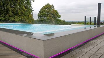 Uma piscina infinita moderna com vista para o oceano, cercada por vegetação exuberante e um deck de madeira.
