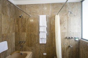 Casa de banho com banheira, chuveiro e um porta-toalhas com vários toalhas.