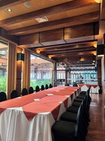 Uma sala de conferência com mesas compridas, cadeiras pretas e teto de madeira.