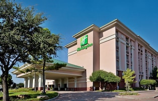 Um hotel Holiday Inn com um edifício grande, área de estacionamento coberta e paisagismo bem cuidado.