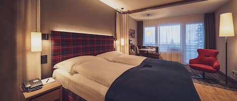 Quarto de hotel com cama, mesa de cabeceira, luminária, cadeira e vista para o exterior.