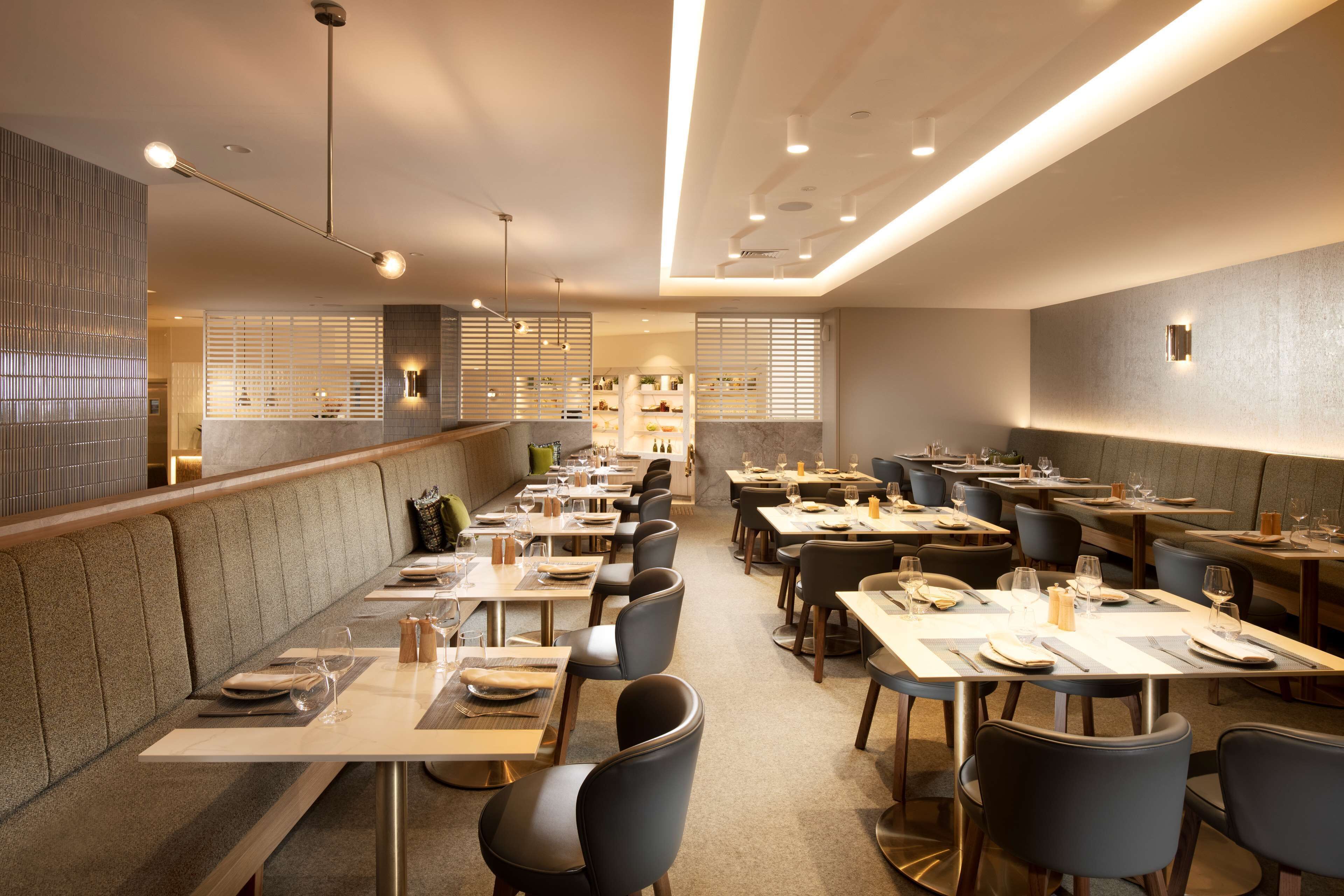 Um restaurante moderno com mesas compridas, assentos acolchoados e um interior limpo e bem iluminado.