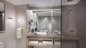Uma casa de banho moderna com um espelho grande, duas lavatórios, chuveiro e estantes embutidas para artigos de higiene pessoal.