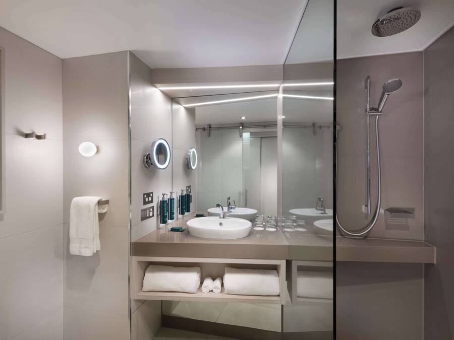 Uma casa de banho moderna com um espelho grande, duas lavatórios, chuveiro e estantes embutidas para artigos de higiene pessoal.