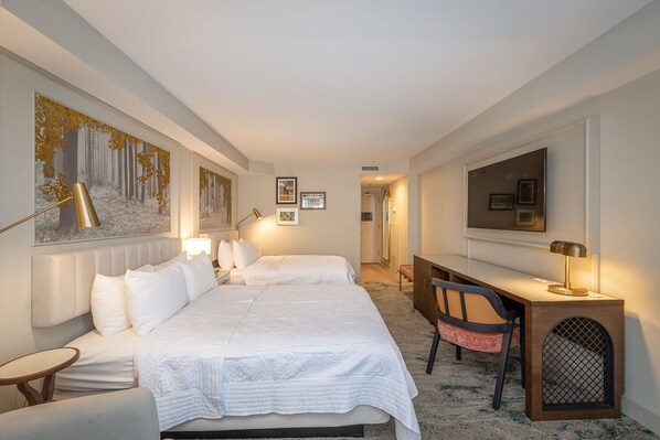 Quarto de hotel com duas camas, uma escrivaninha, uma cadeira e um quadro grande na parede.
