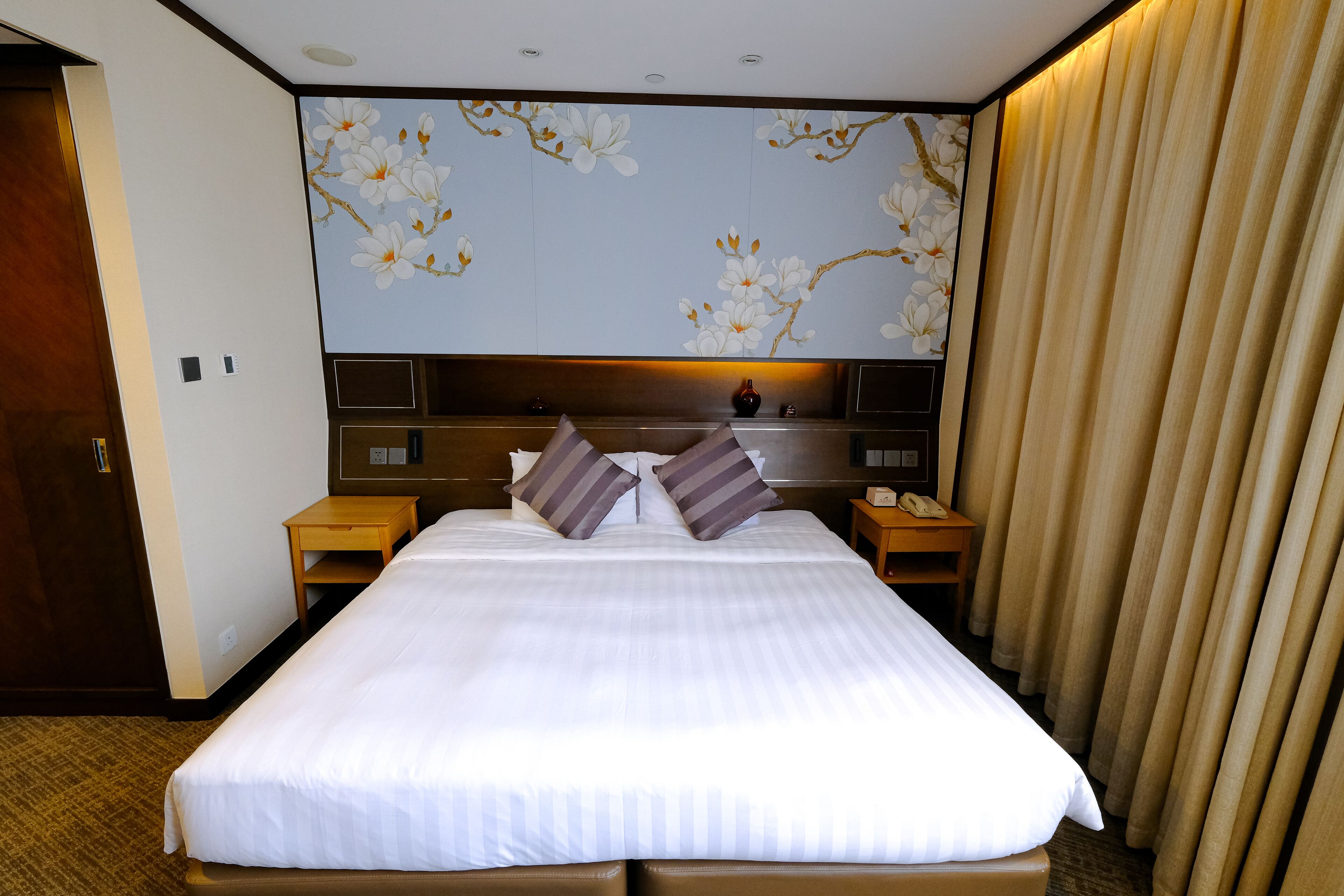 Quarto de hotel com uma cama grande, cabeceira de madeira e um mural floral na parede.