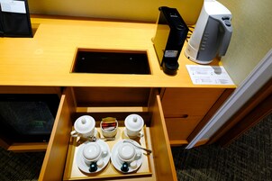 Quarto de hotel com escrivaninha de madeira, máquina de café, chaleira e bandeja com bules, xícaras e pires.