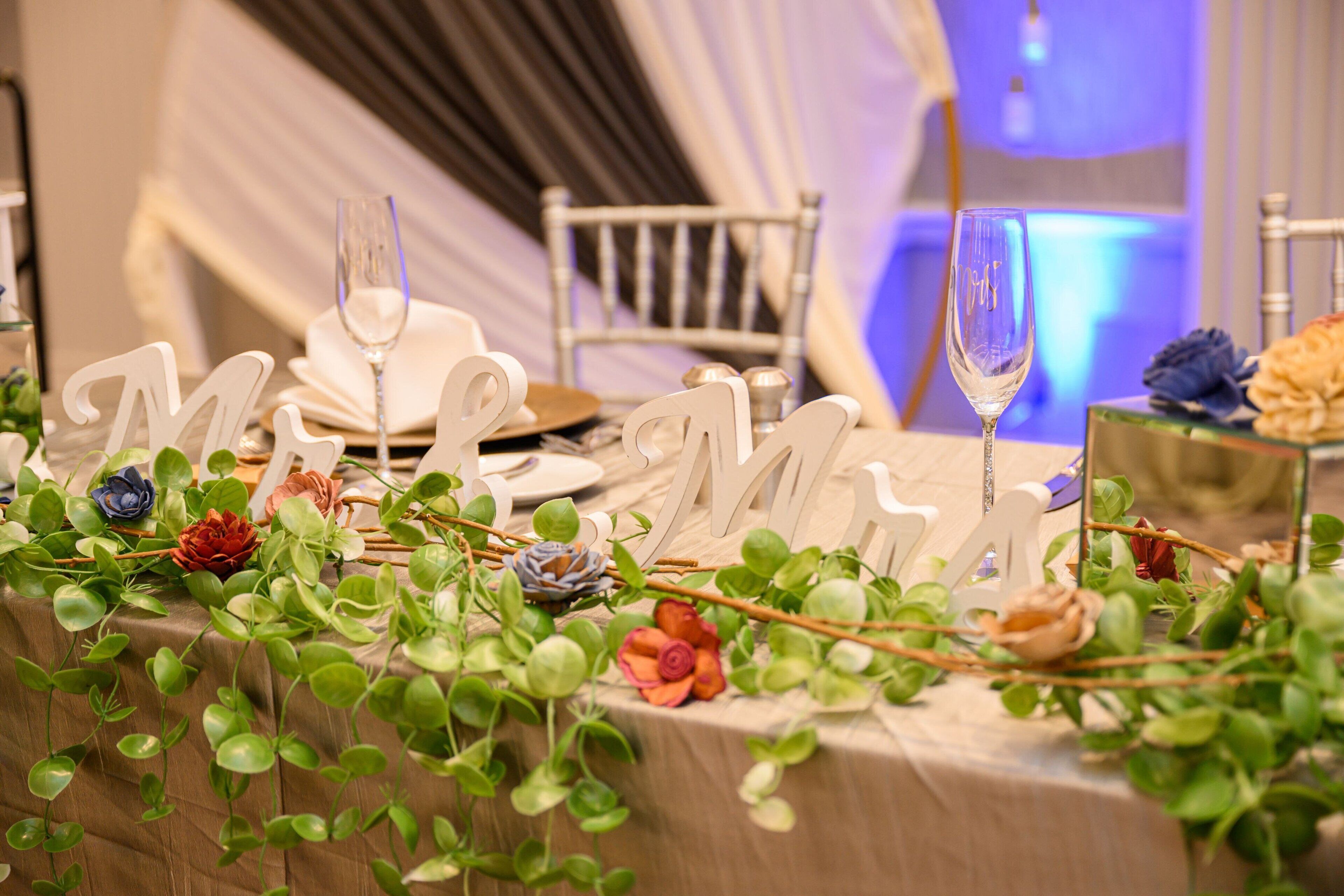 Uma mesa posta com decoração em letras brancas, folhagem verde e algumas flores.