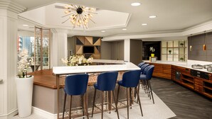 Uma cozinha moderna com bancada, banquetas e uma luminária decorativa no teto.