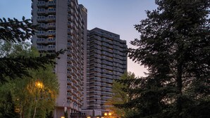 Um edifício alto com vários andares, rodeado por árvores e um jardim bem cuidado.