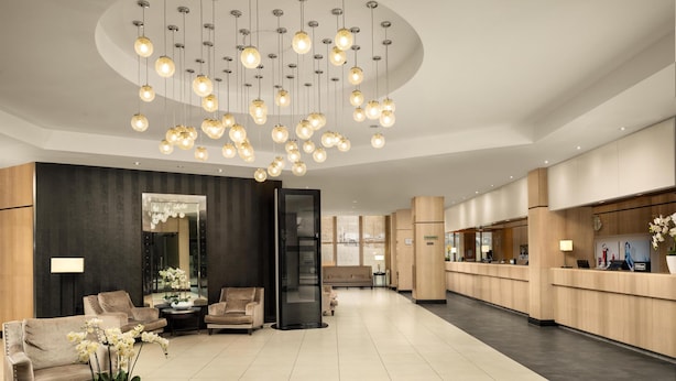 Um lobby moderno de hotel com uma receção, área de estar e um candelabro grande.