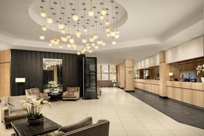 Um lobby moderno de hotel com uma receção, área de estar e um candelabro grande.