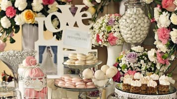 Uma mesa com diversos doces e arranjos florais, incluindo uma placa com a inscrição "FIESTA AMERICANA".