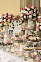 Uma mesa com diversos doces e arranjos florais, incluindo uma placa com a inscrição "FIESTA AMERICANA".