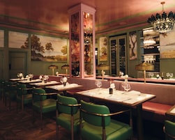 Interior de restaurante com cadeiras estofadas em verde, mesas de madeira e um candelabro.