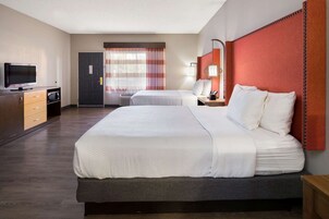 Quarto de hotel com uma cama grande, televisão, escrivaninha com luminária e janela com cortinas.