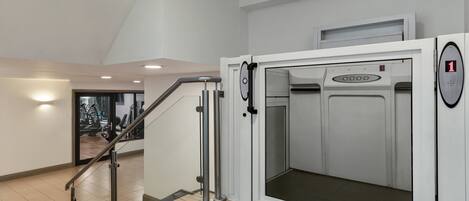 Um elevador moderno com mostrador digital, corrimão de metal e porta de vidro.