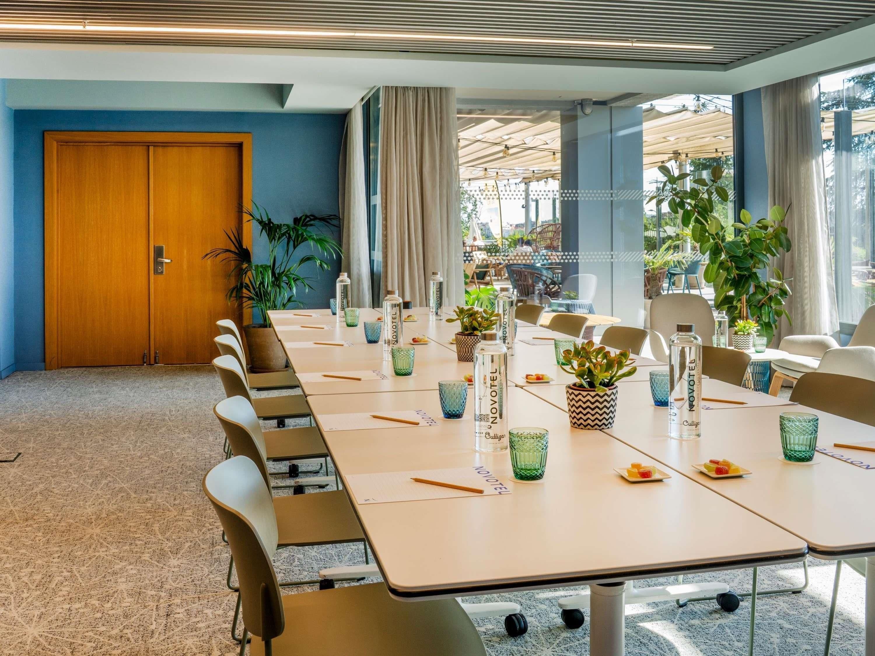 Uma sala de conferências com uma mesa comprida, cadeiras e plantas em vasos.