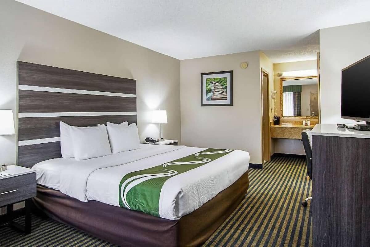 Quarto de hotel com uma cama grande, escrivaninha, cadeira, espelho e televisão.