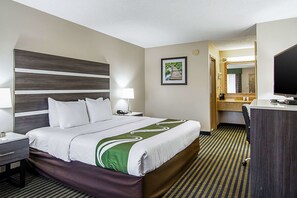 Quarto de hotel com uma cama grande, uma mesa, uma cadeira, um espelho e uma televisão.