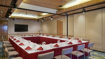 Uma sala de conferências com uma mesa comprida preparada para uma reunião, equipada com cadeiras e uma televisão de tela plana.