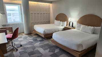 Quarto de hotel com duas camas, uma escrivaninha, uma cadeira e um tapete estampado.
