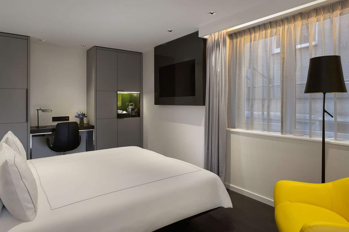 Quarto de hotel com cama, escrivaninha, cadeira, televisão e janela com cortinas.