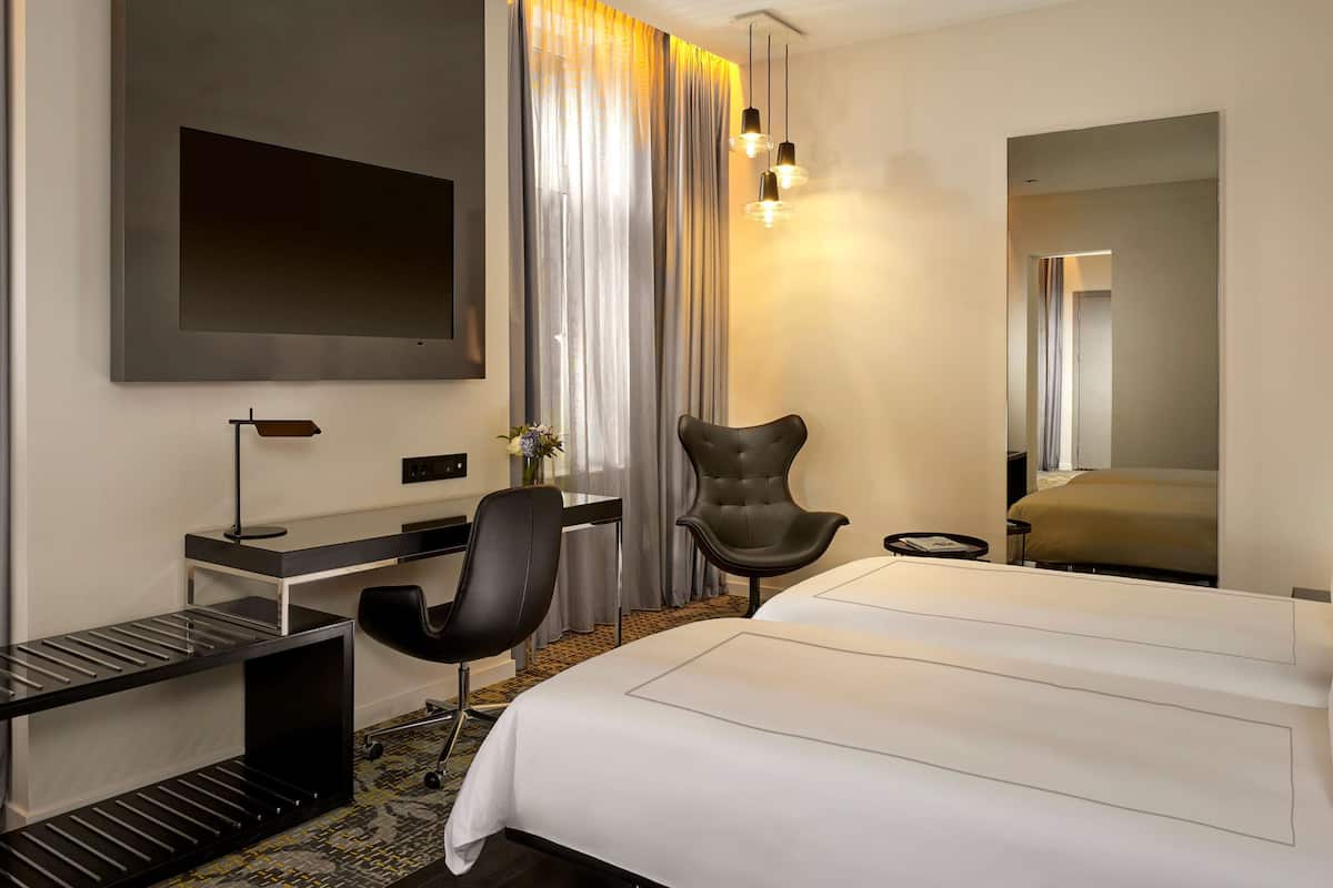 Quarto de hotel moderno com uma cama grande, uma mesa com cadeira, uma TV de tela plana e um espelho amplo.