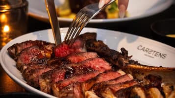 Uma pessoa cortando bife em um prato com garfo e faca.