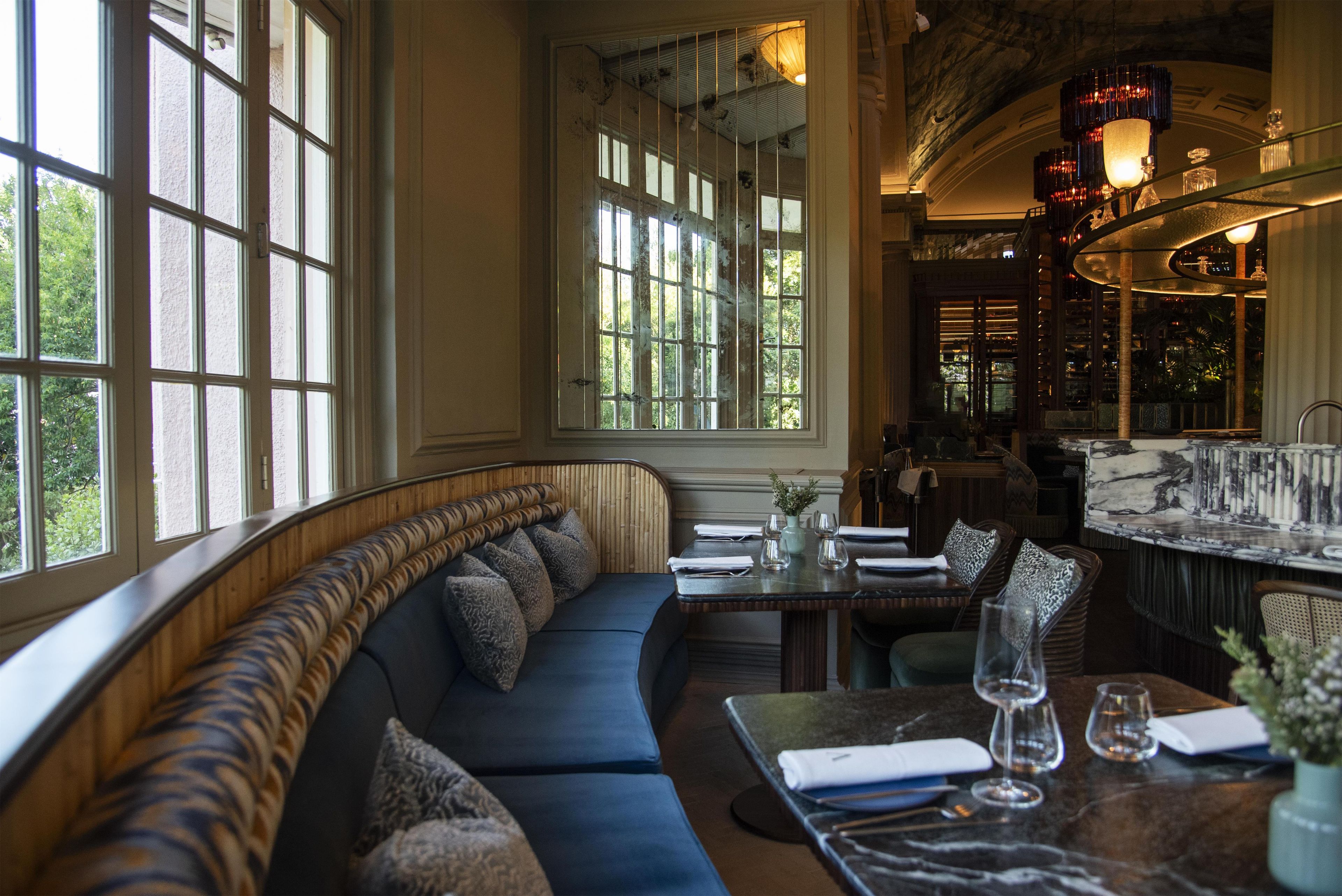Restaurante com área de estar em um banco de madeira curvado, janelas amplas e balcão de bar em mármore.