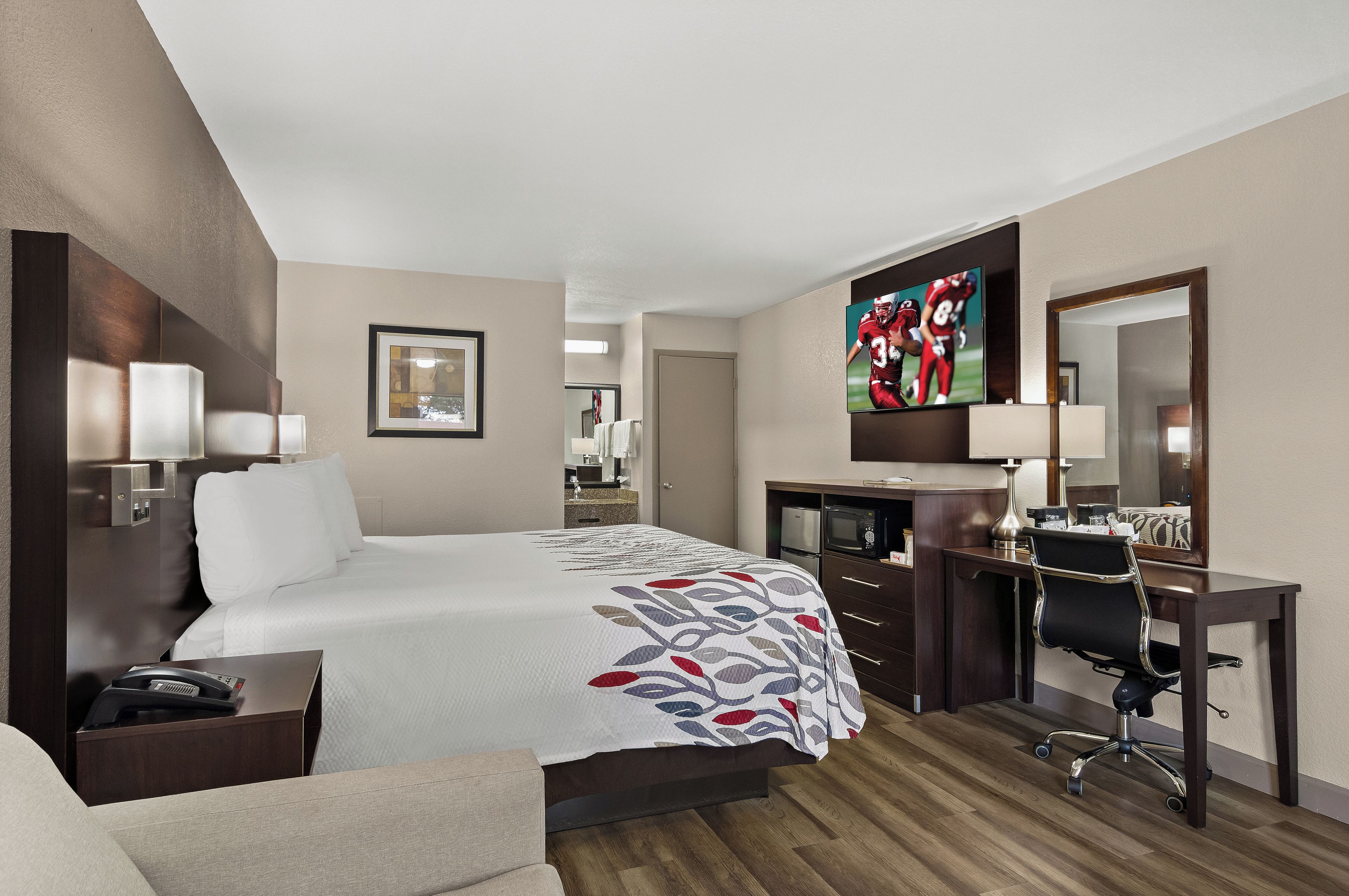 Quarto de hotel com uma cama grande, uma mesa com cadeira, uma TV e um espelho.