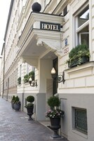Hotel com fachada clássica, placa e vasos de plantas.