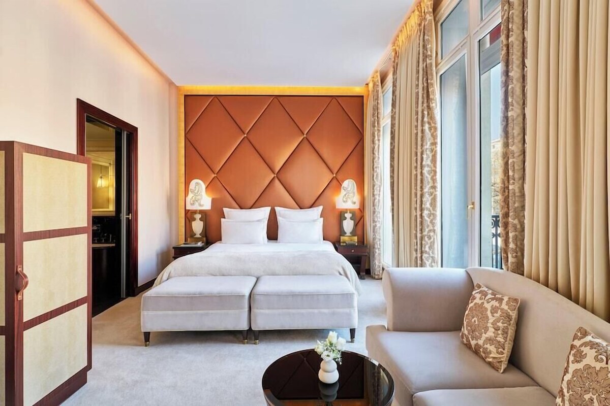 Quarto de hotel com uma cama grande, um sofá, uma mesa de centro e uma cabeceira decorativa.