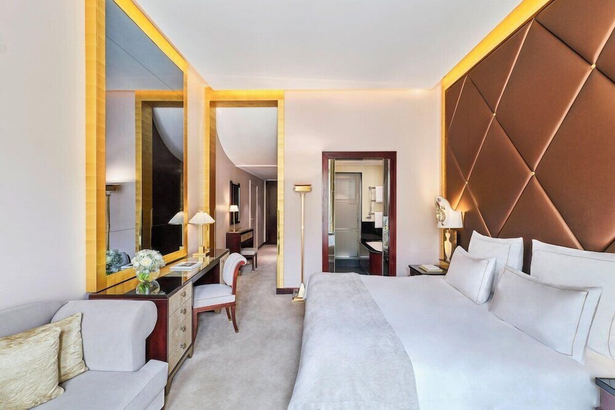 Quarto de hotel com uma cama grande, uma escrivaninha com cadeira, um espelho e um guarda-roupa.