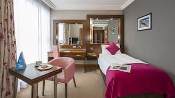 Quarto de hotel com cama, escrivaninha, cadeira, espelho e janela com cortinas.