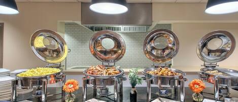 Disposição de buffet com diversos alimentos e utensílios de servir.