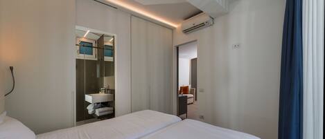 Quarto de hotel com duas camas, banheiro com espelho e ar condicionado.