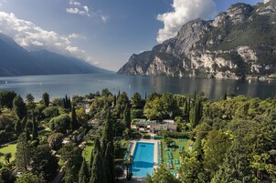 Um resort com piscina, vegetação exuberante e vista para um lago e montanhas.