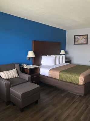 Quarto de hotel com cama, cadeira, mesa de cabeceira e abajur.