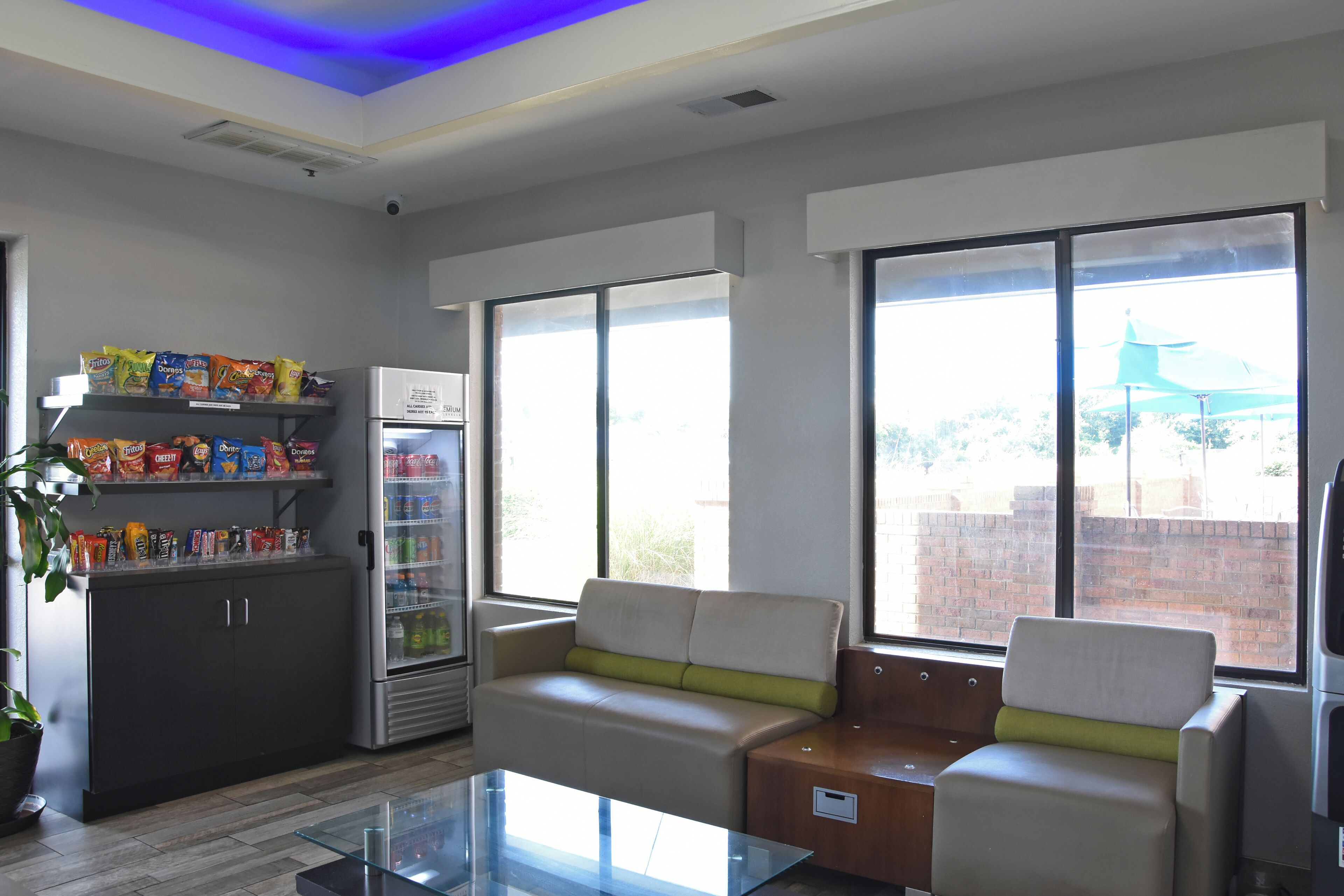 Uma área de espera moderna com sofá, mesa de vidro, máquina de vendas automática e frigorífico.