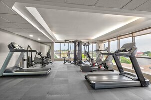 Academia com esteiras, aparelhos de musculação e vista para o exterior.