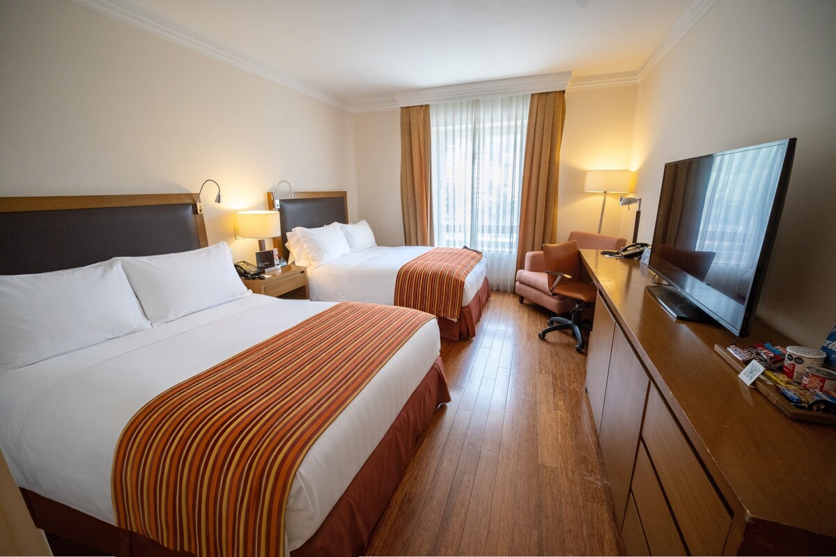 Quarto de hotel com duas camas, televisão, escrivaninha e uma cadeira.
