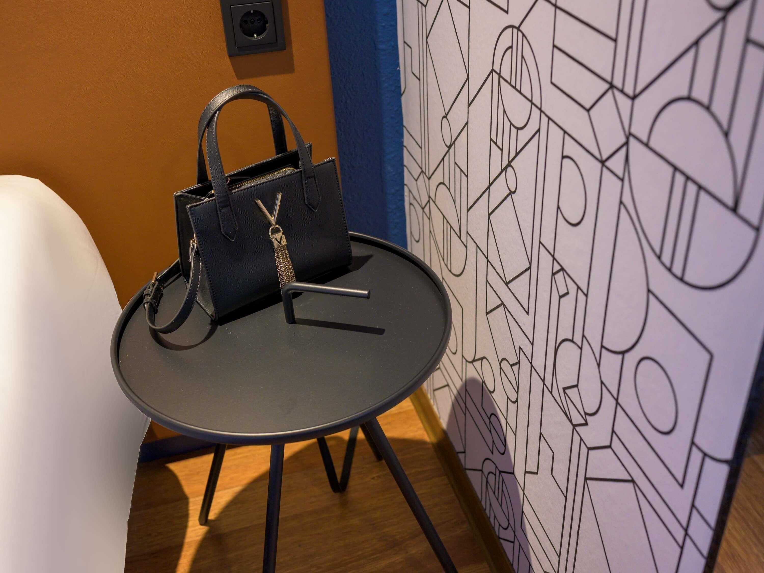 Uma bolsa preta sobre uma pequena mesa redonda, com um design geométrico no fundo.