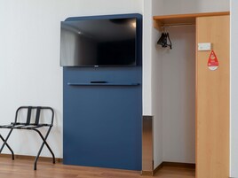 Quarto com televisão de tela plana fixada num armário azul, uma porta de madeira com um adesivo vermelho e uma cadeira preta.