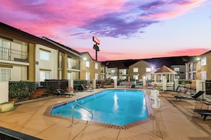 Piscina com espreguiçadeiras e céu ao pôr do sol.