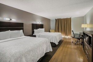 Quarto de hotel com duas camas, uma escrivaninha, uma cadeira e uma janela com cortinas.