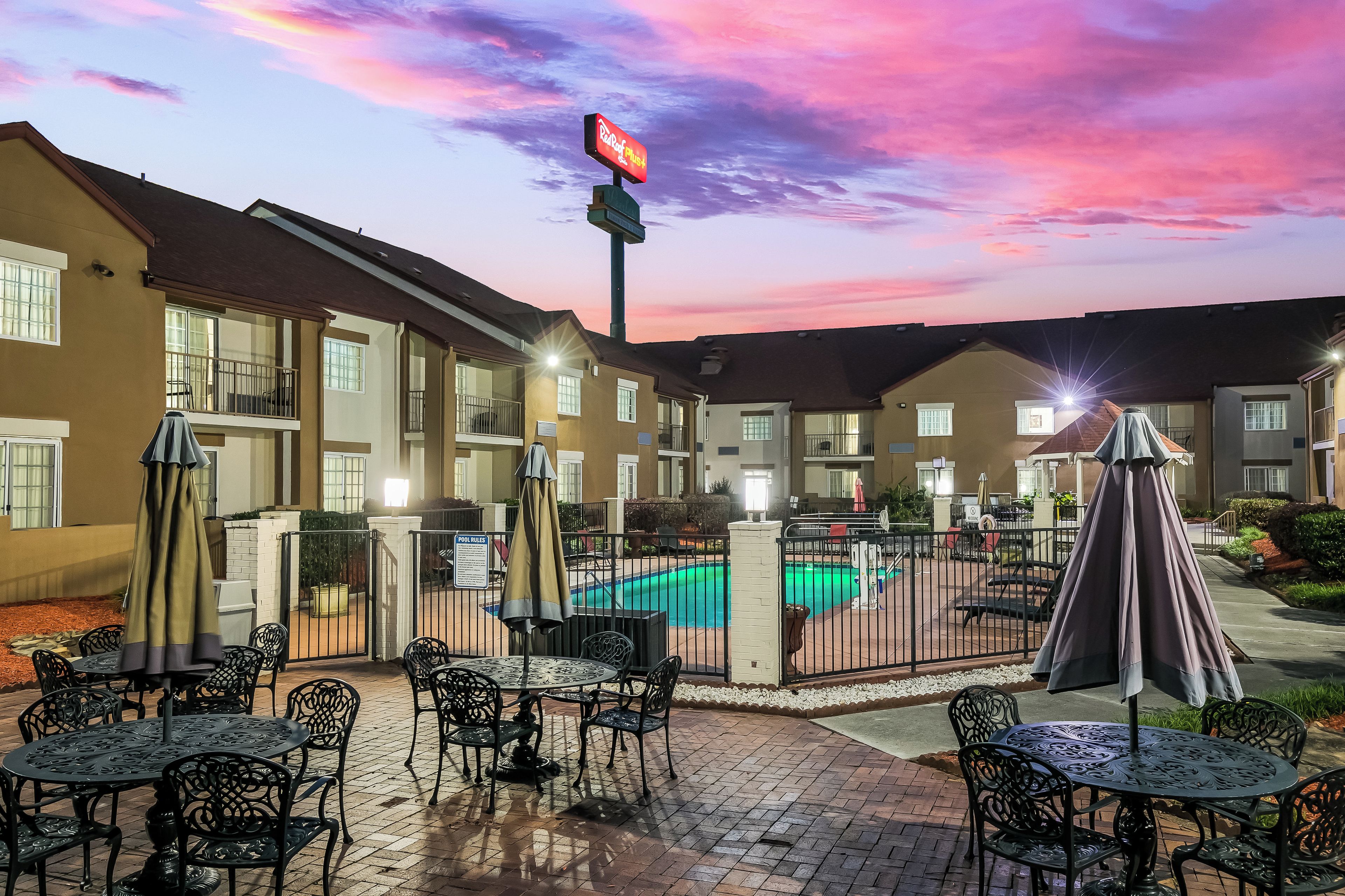 Pátio de hotel com área de estar externa, piscina e céu ao pôr do sol.