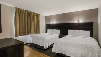 Quarto de hotel com duas camas, cômoda de madeira, janela com cortinas e luminária na parede.